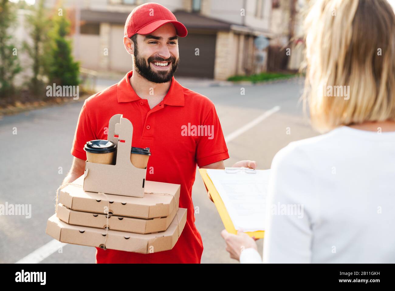 Image of smiling delivery man in red uniform giving food order to ...