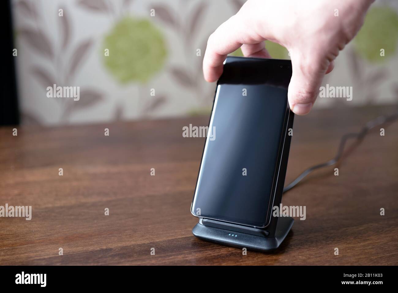 smartphone wireless charging on charging stand on wooden table. male ...