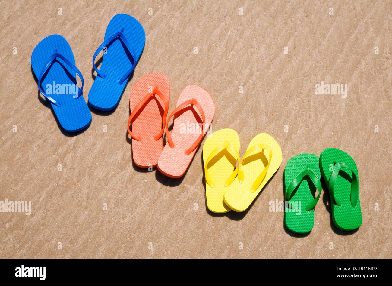 Group of flip-flops in bright summer colors sitting on smooth sand ...