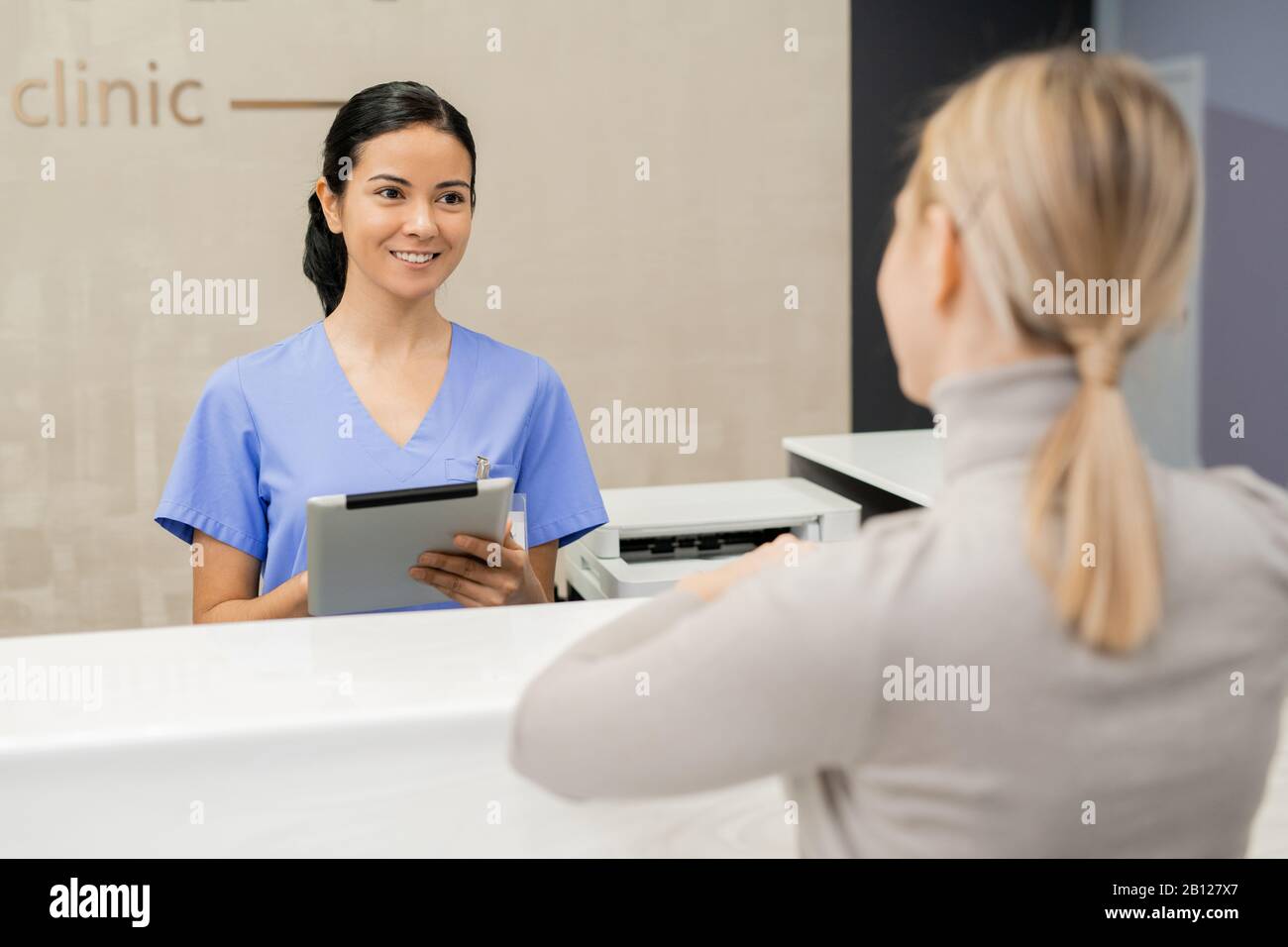 Happy young assistant standing by reception counter in front of patient ...