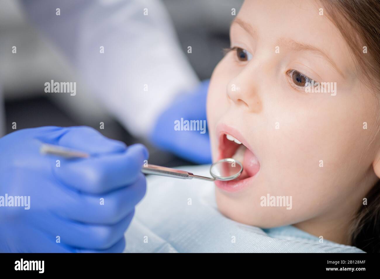 Gloved hand of dentist examining teeth of little girl with her mouth ...