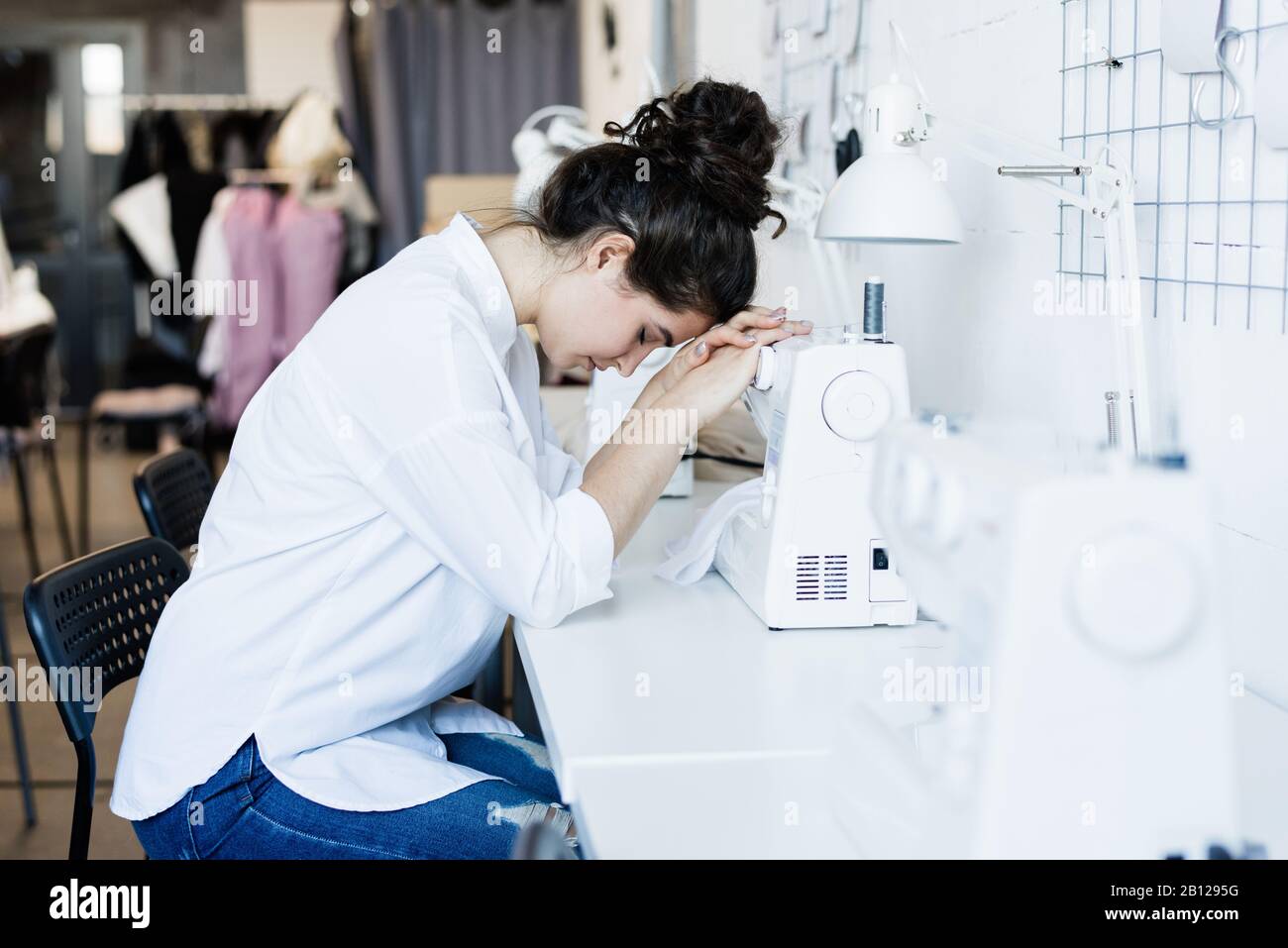 Young tired or sick seamstress keeping her head on electric sewing ...