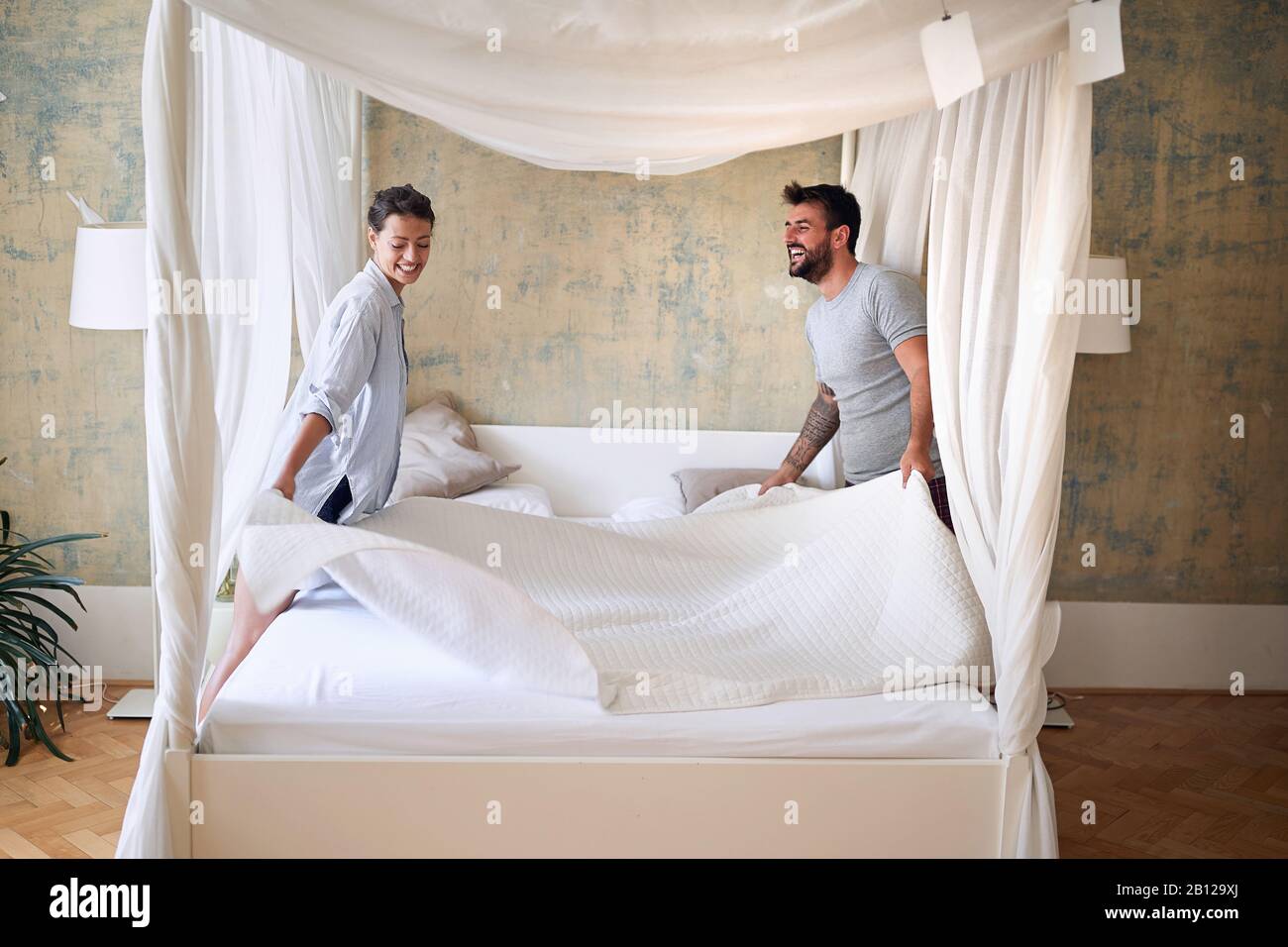 couple smiling, laughing while making bed together in the morning in ...
