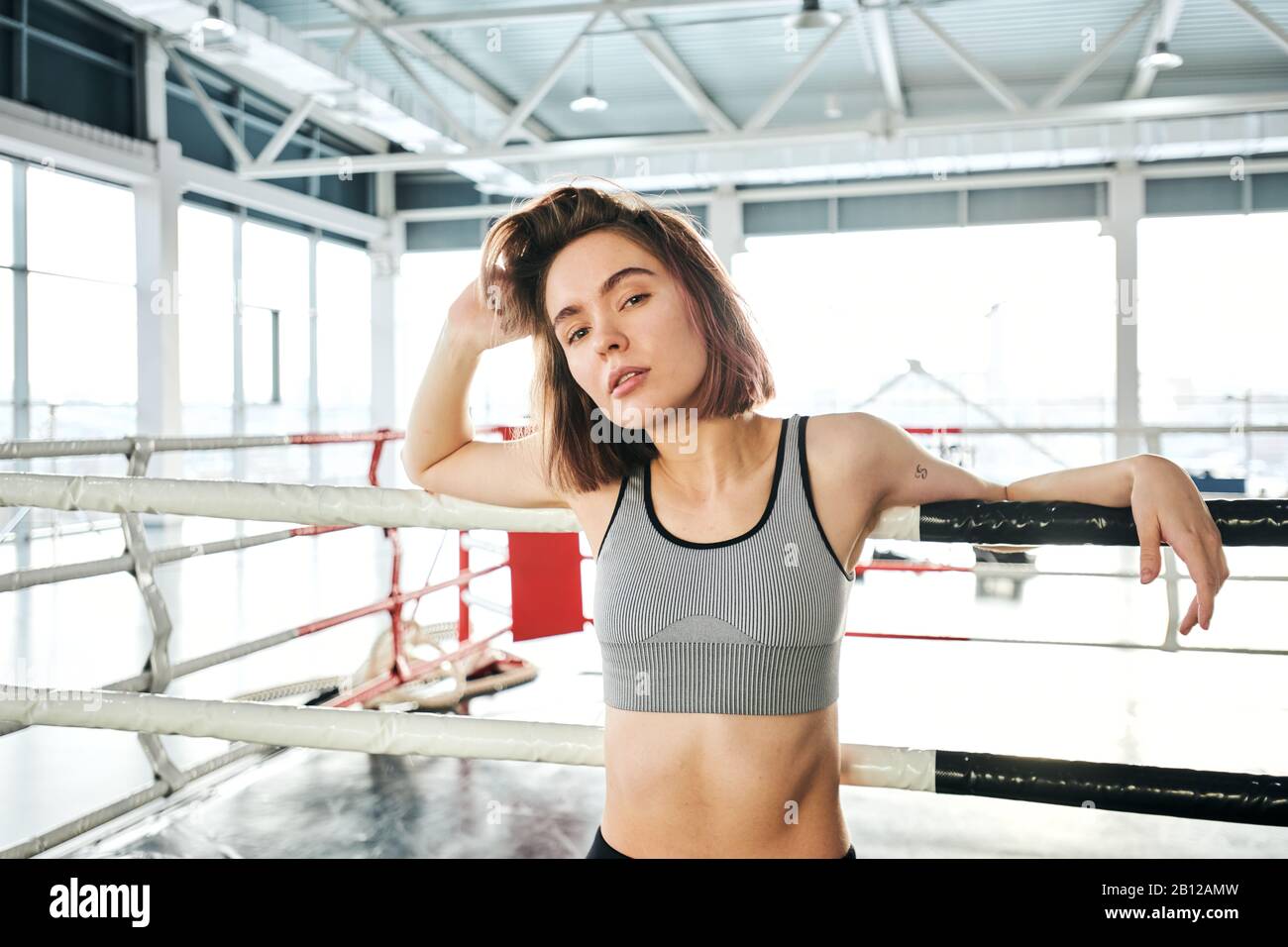 Pretty young sportswoman in grey tracksuit standing by boxing ring ...