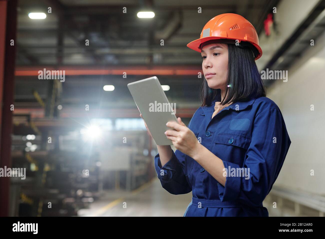 Female engineer in hardhat and blue uniform working with technical data ...