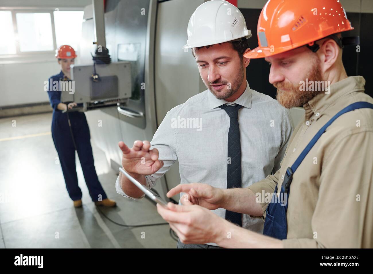 Two young male engineers pointing at technical data on tablet display ...