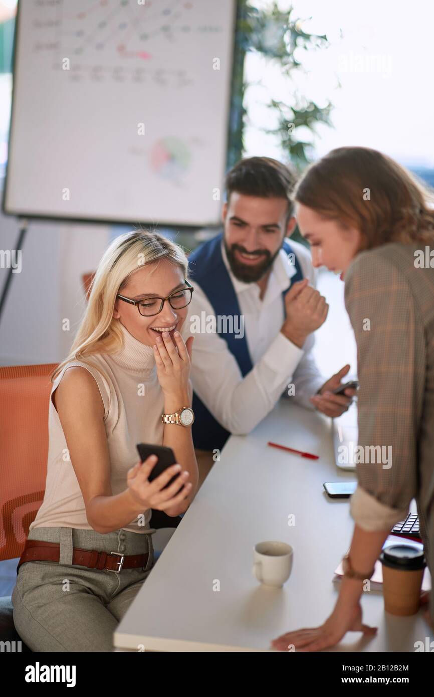 colleagues sharing funny content from a cell phone on work. casual ...