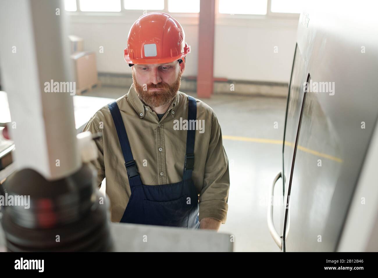 Young serious engineer with beard standing in front of control panel in ...