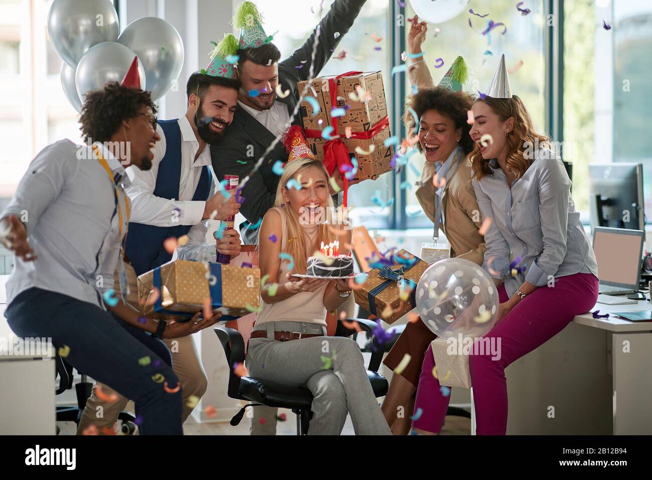 group of colleagues surprising female colleague with birthday cake at ...