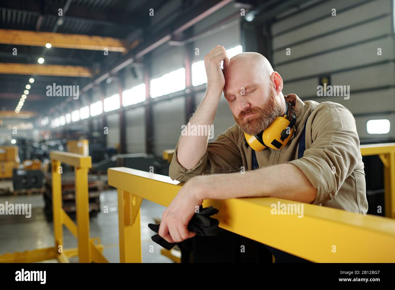 Tired or sick bald engineer touching his head while leaning by bar at ...