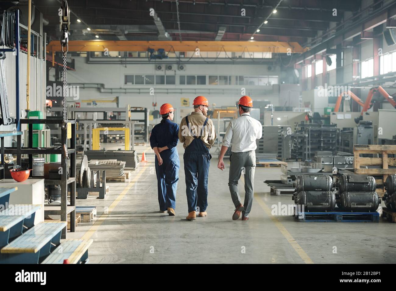 Back view of three workers of industrial plant walking along large ...