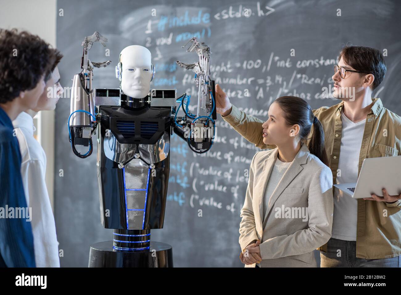 Group of students looking at computer control robot with raised hands ...