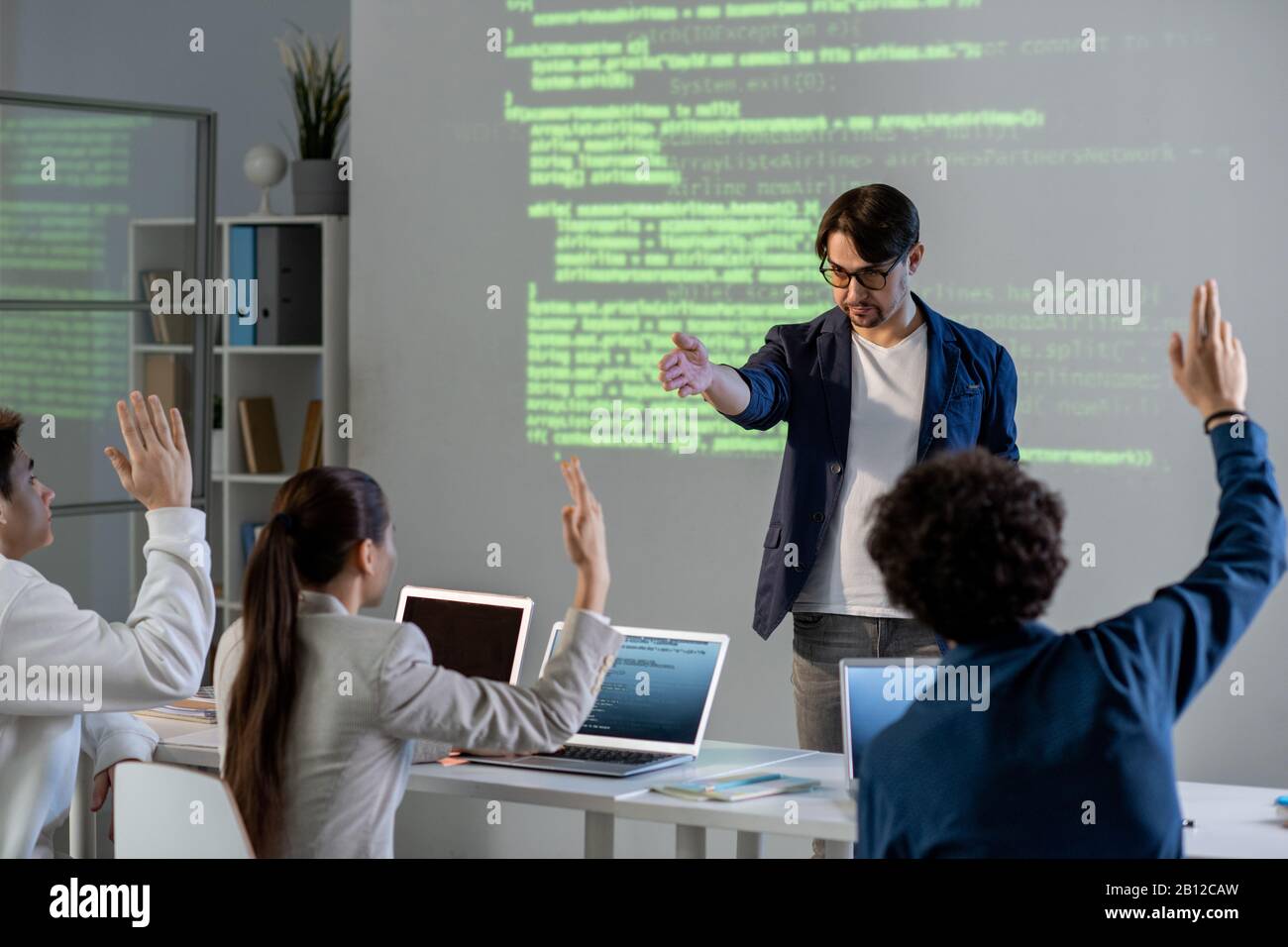 Confident male teacher pointing at one of students on the first row ...