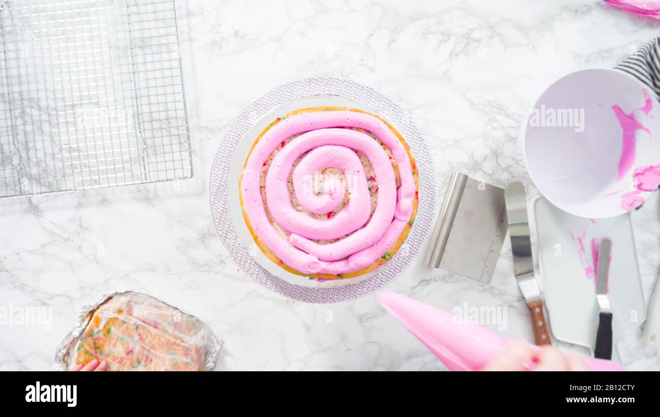 Flat lay. Step by step. Frosting round funfetti cake layers with pink ...