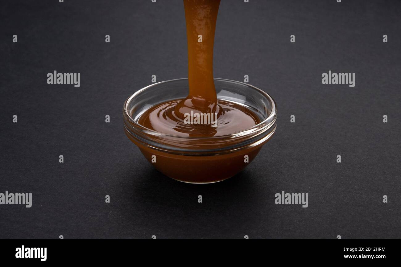 Pouring caramel sauce on black background Stock Photo - Alamy