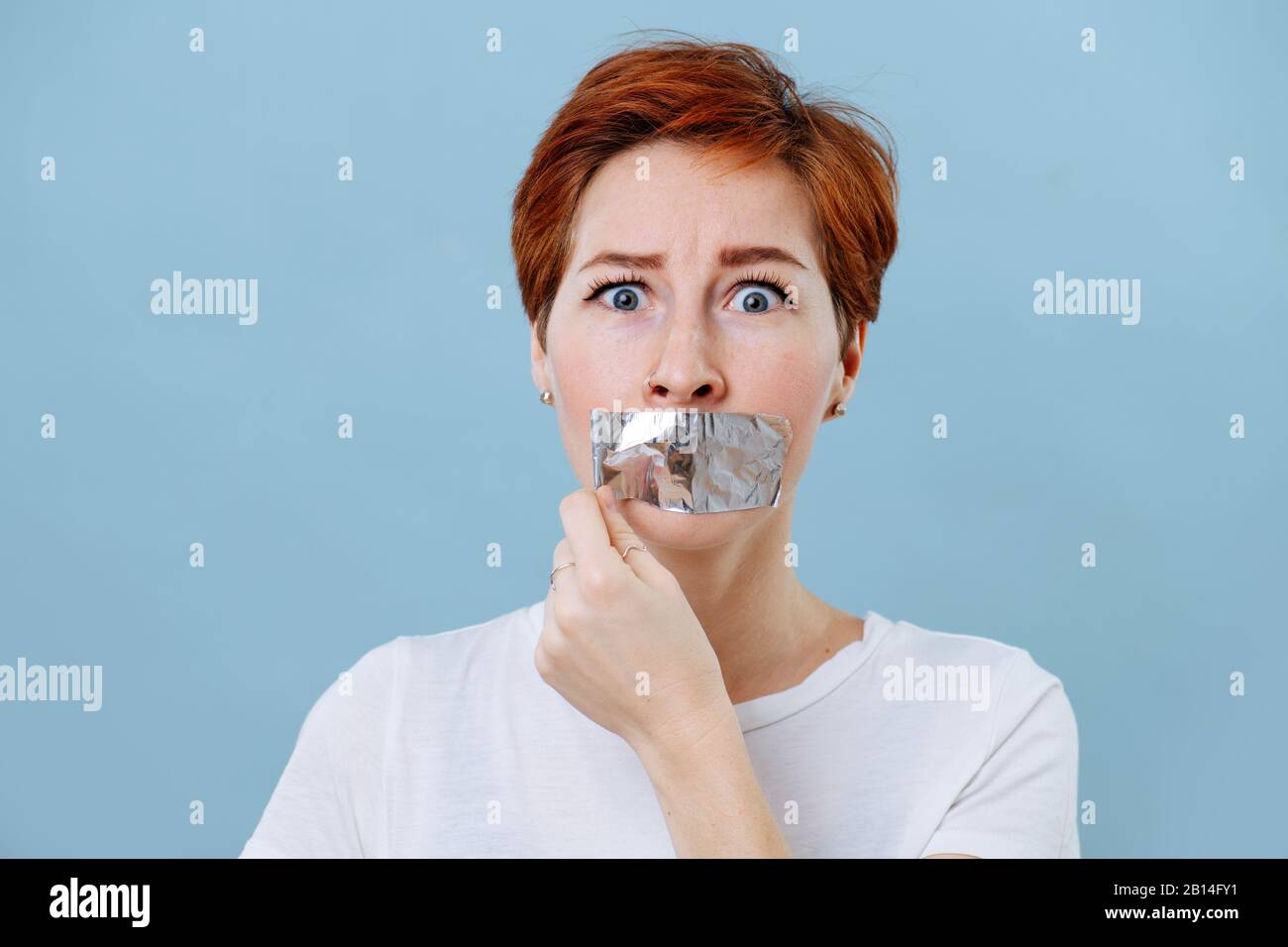 Portrait of a frightened woman with short ginger hair and mouth taped ...
