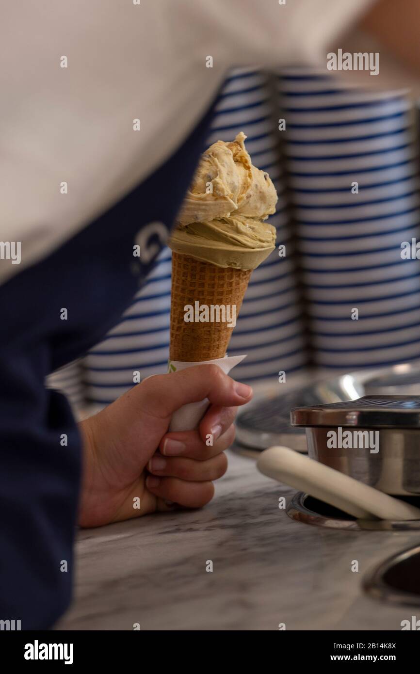 Hand holding waffle cone and scooping ice cream into it, restaurant ...