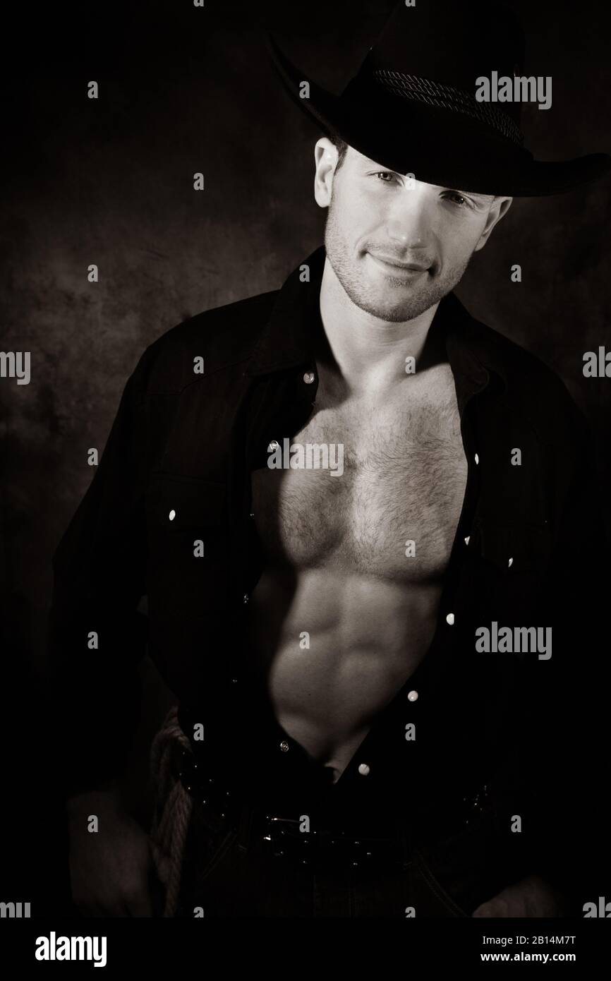 Portrait of attractive cowboy looking at camera with hat and open black ...