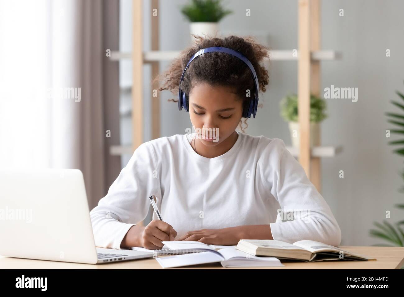 Focused african african teen girl wearing headphones writing notes ...