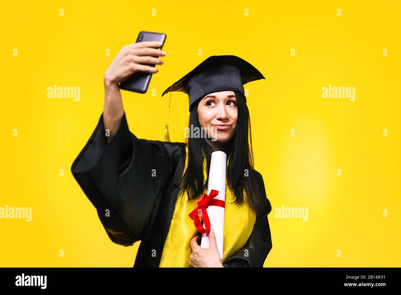 graduate woman makes selfie photo on phone over yellow background ...