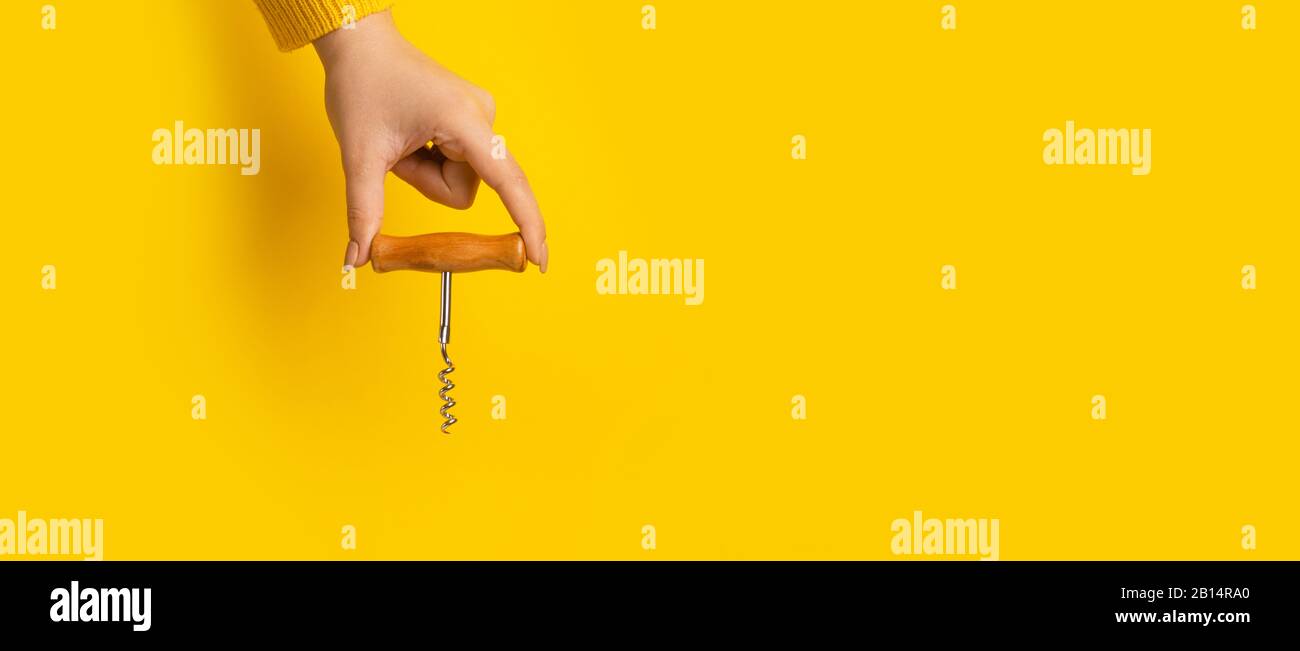female hand holding corkscrew with wooden handle over yellow background ...