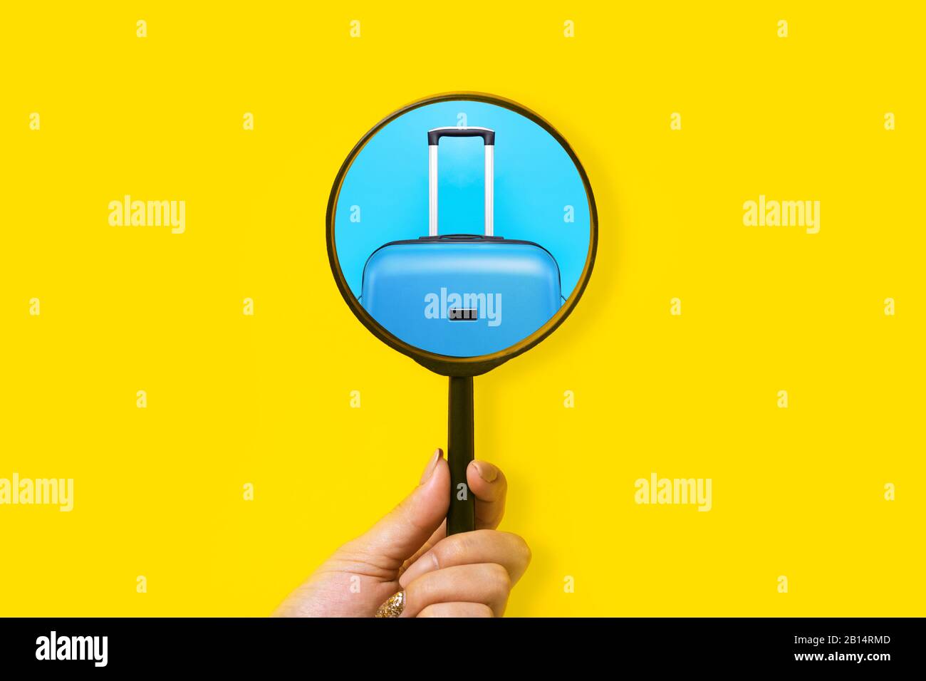 hand holding magnifier over blue suitcase, search places to travel ...