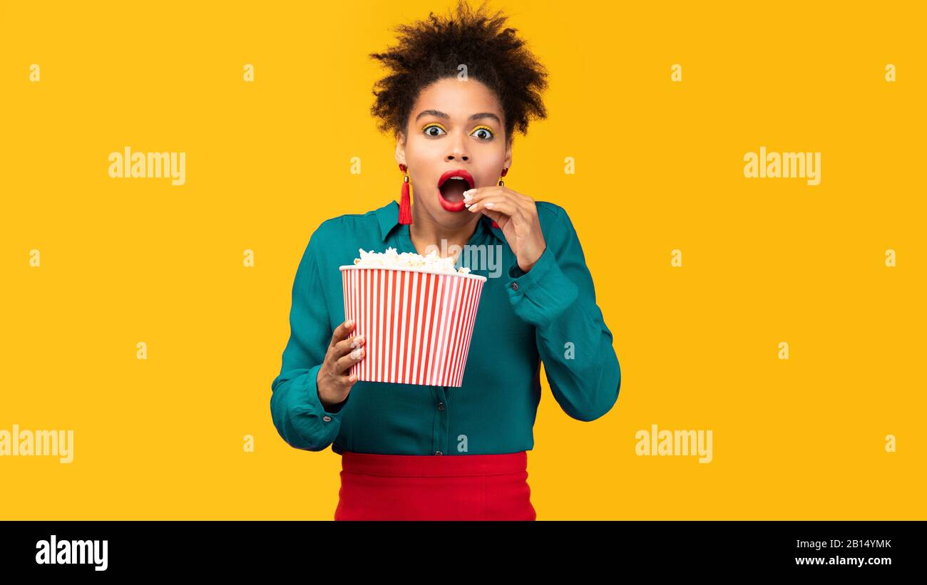 Shocked afro girl eating popcorn staring at camera Stock Photo - Alamy