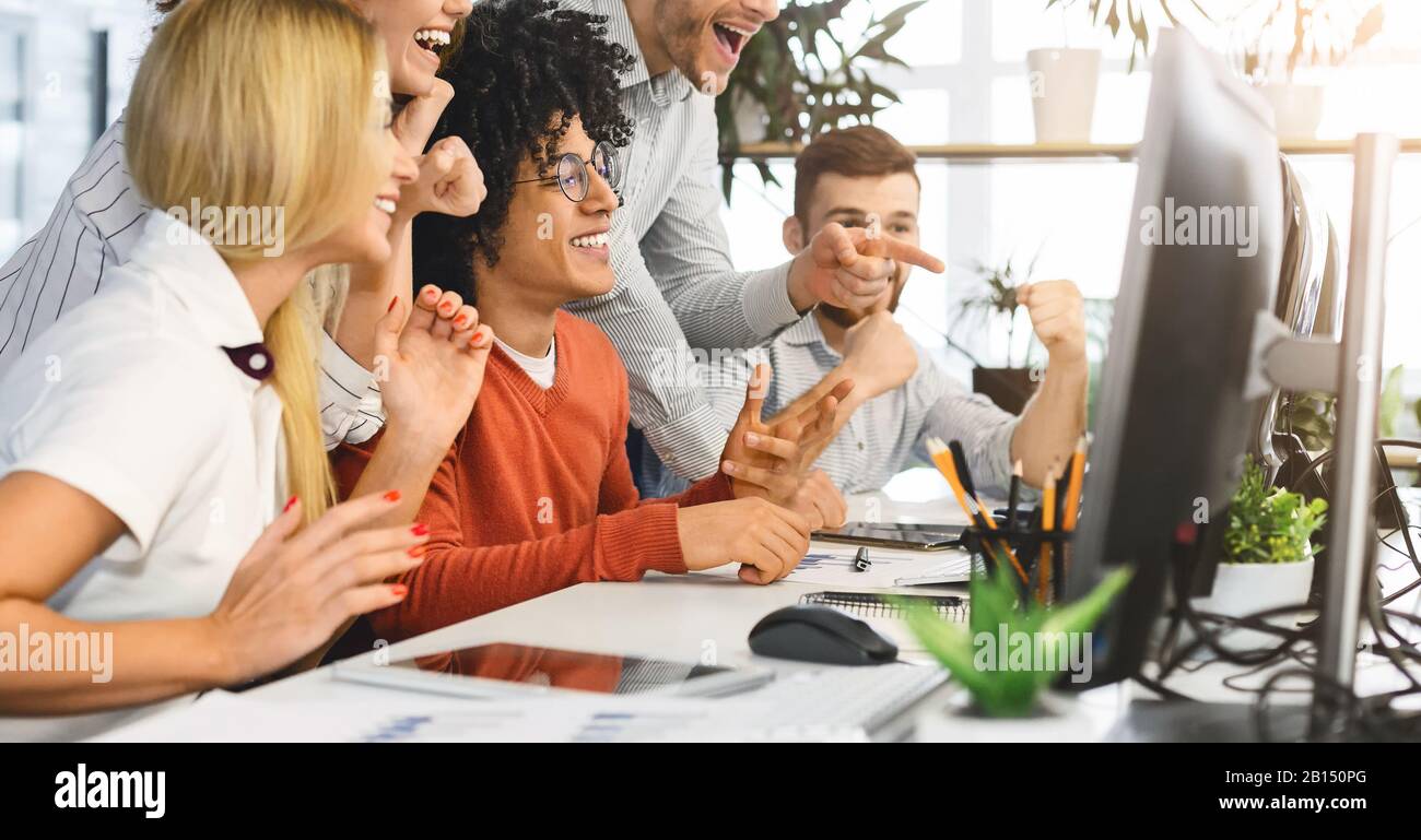 Happy young team celebrating professional success, looking at laptop ...