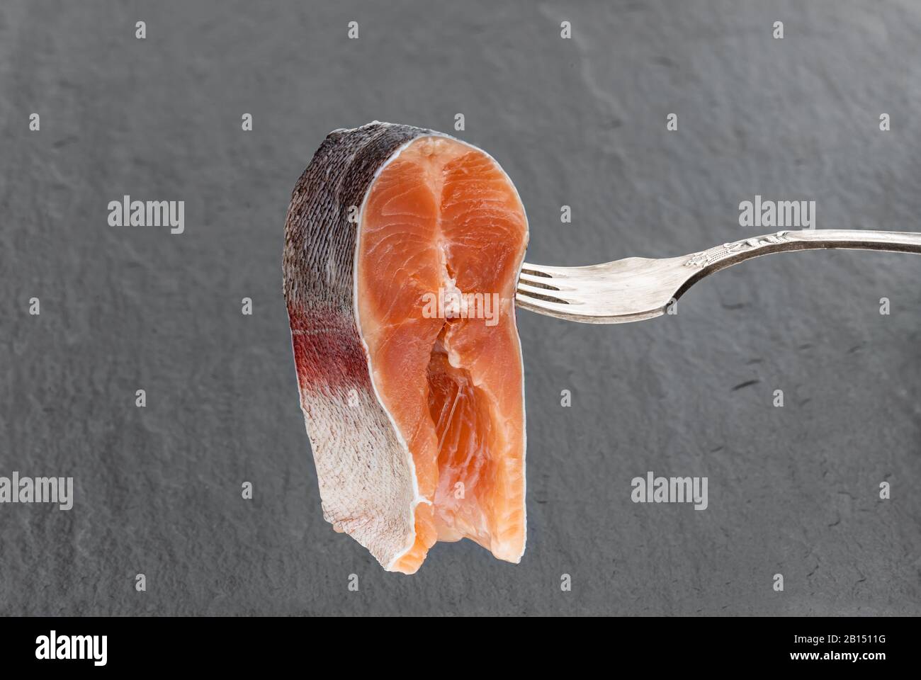 Salted slice of rainbow trout on a fork on black stone background Stock ...
