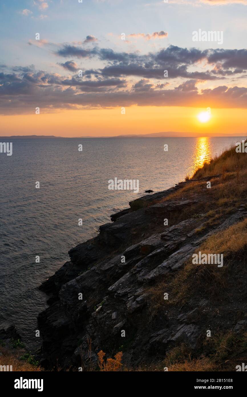 High rocky cliffs by the sea with colorful warm sunset beneath the ...