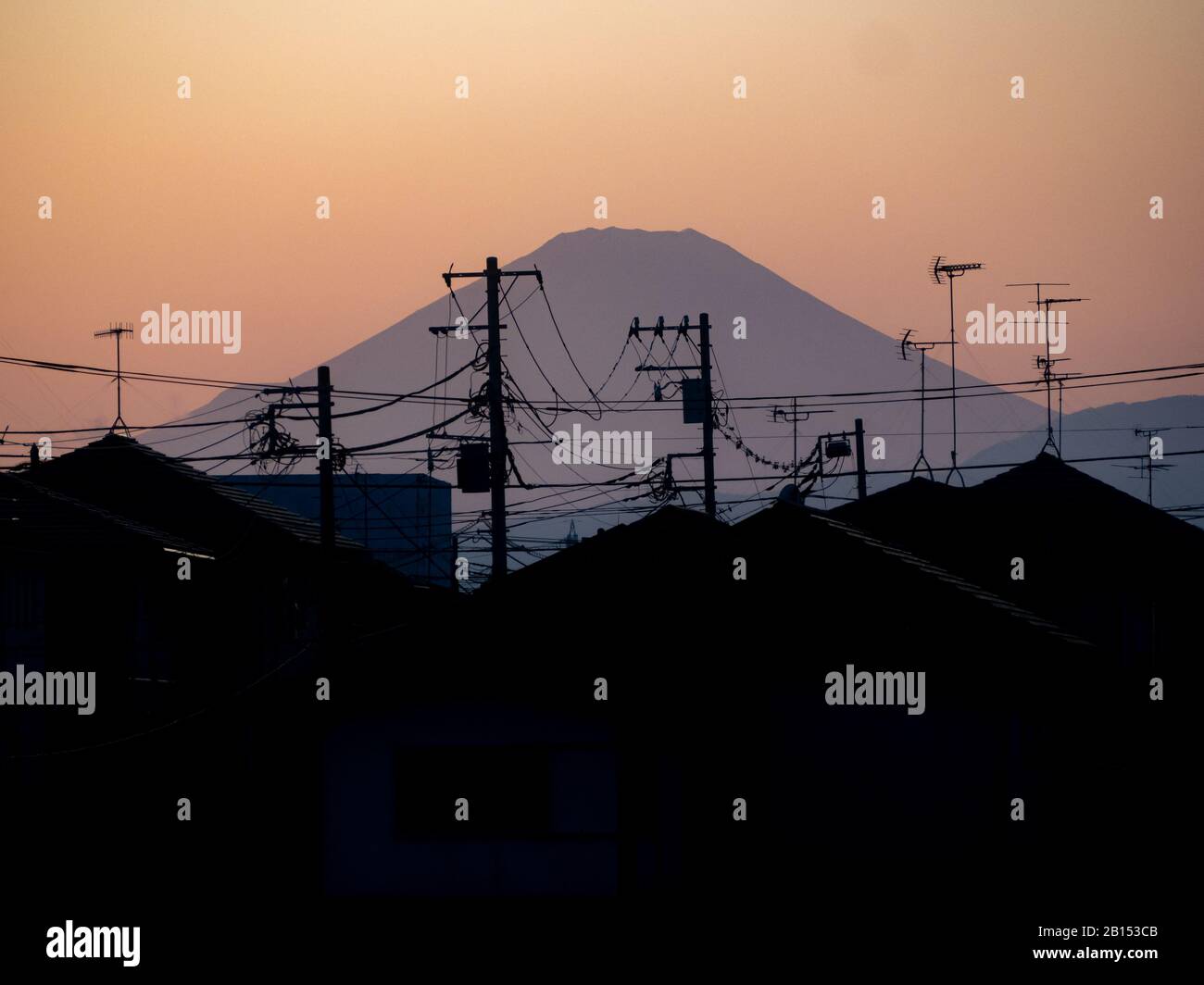 A silhouette of Mt Fuji seen through the power lines and buildings of ...