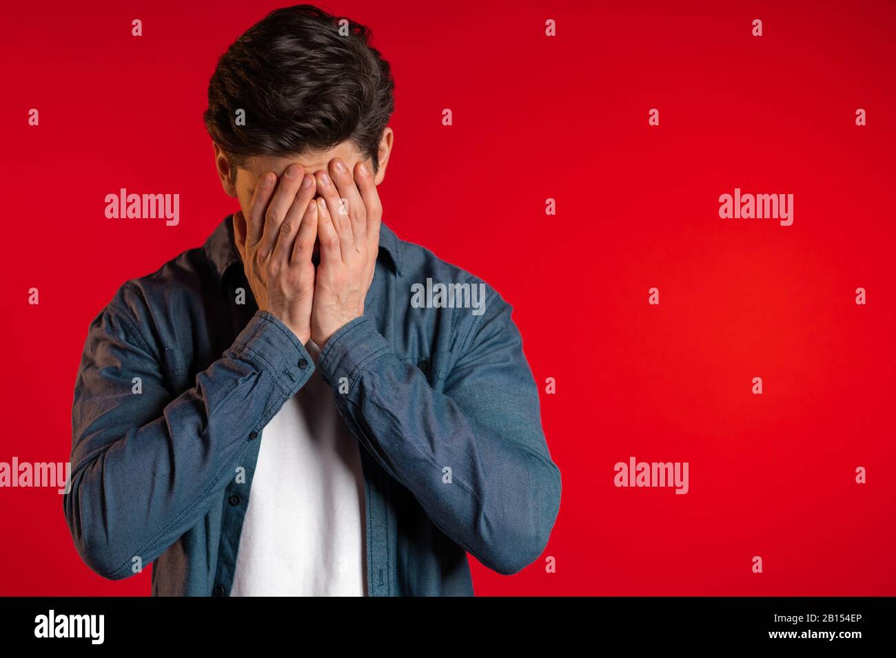 Young guy covers his face with hand from fatal disappointment, failure ...