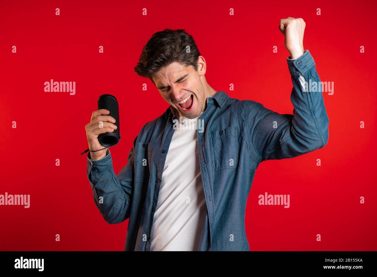 Man smiling, dancing with wireless portable speaker in studio on red ...