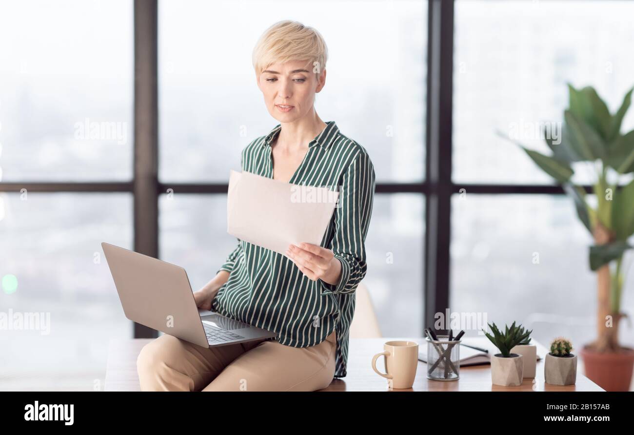 Lady With Laptop Reading Papers Sitting On Desk In Office Stock Photo ...