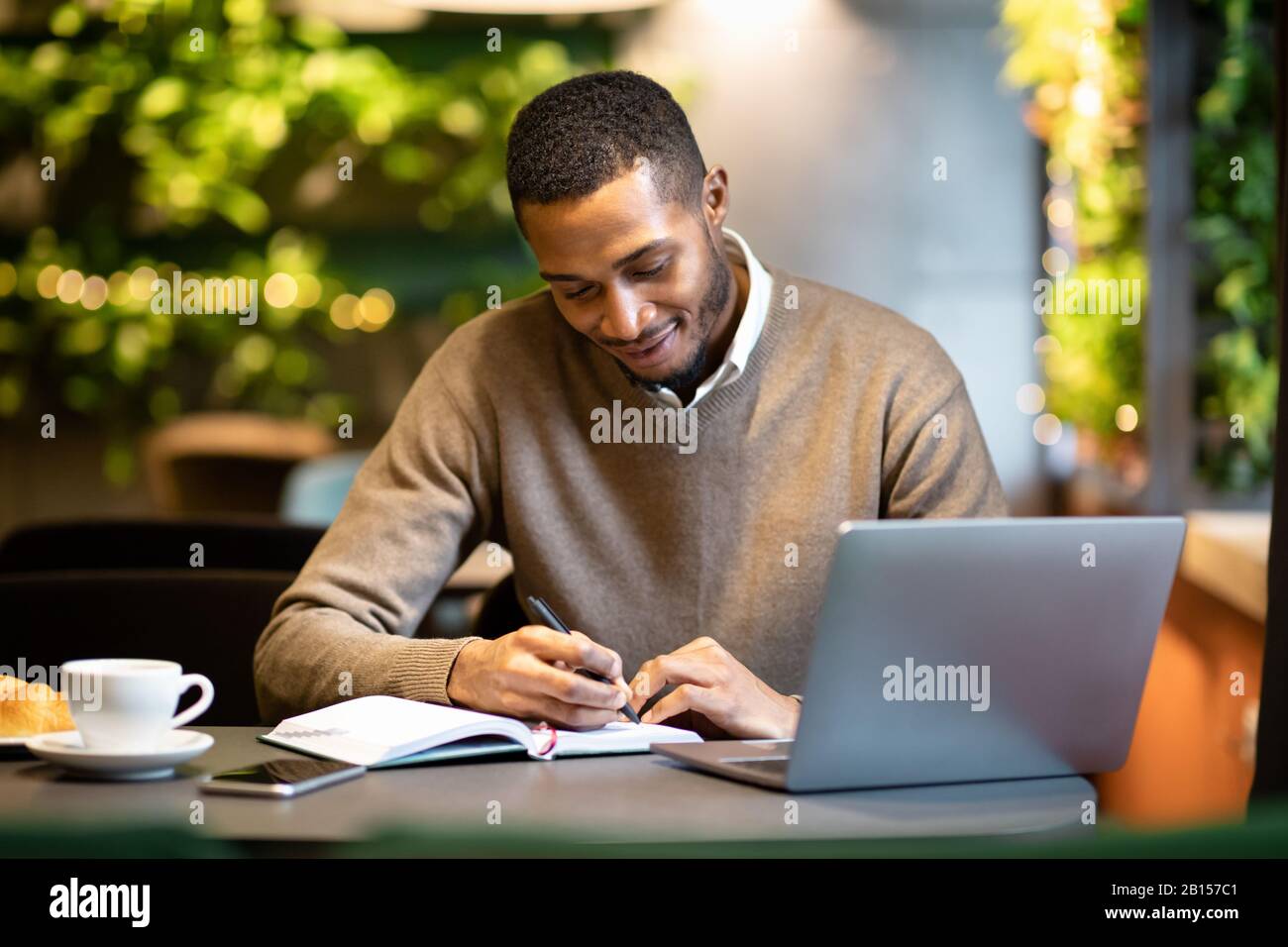 Casual afro man taking notes sitting in cafe Stock Photo - Alamy