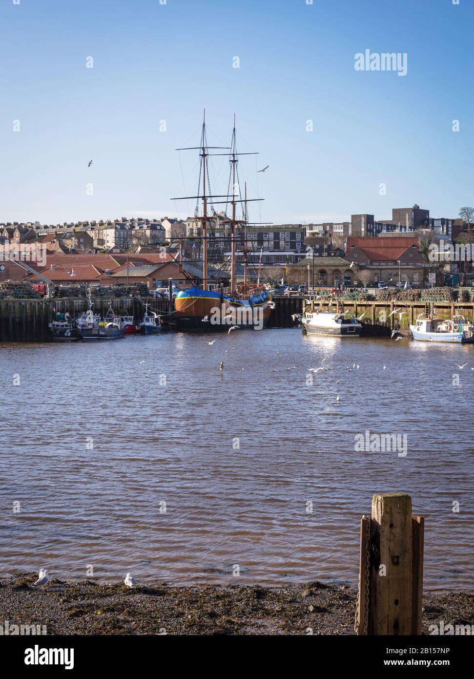 Whitby harbour on a sunny day. Boats are moored to a wharf alongs with ...