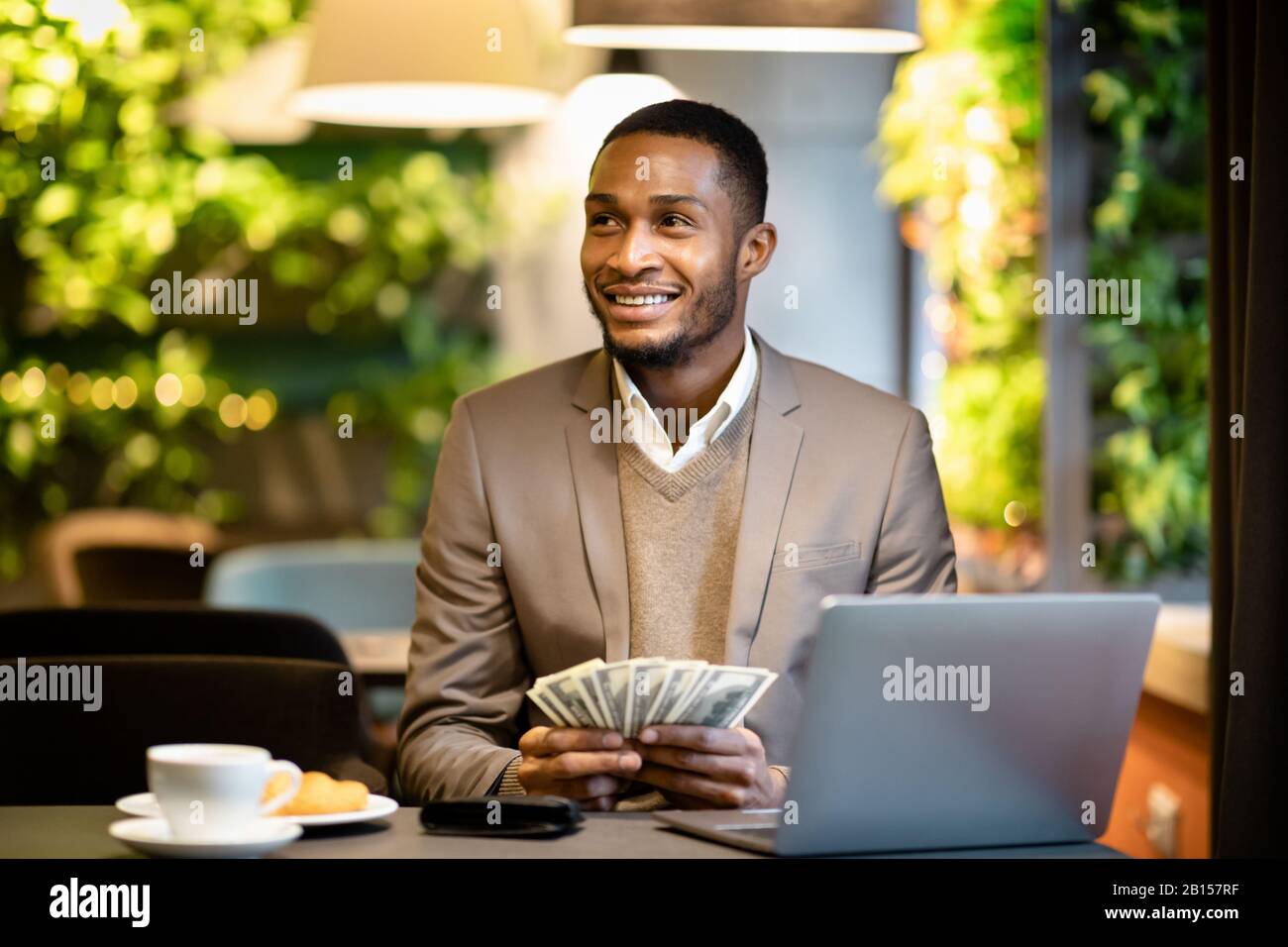 Happy young black man holding money looking away Stock Photo - Alamy