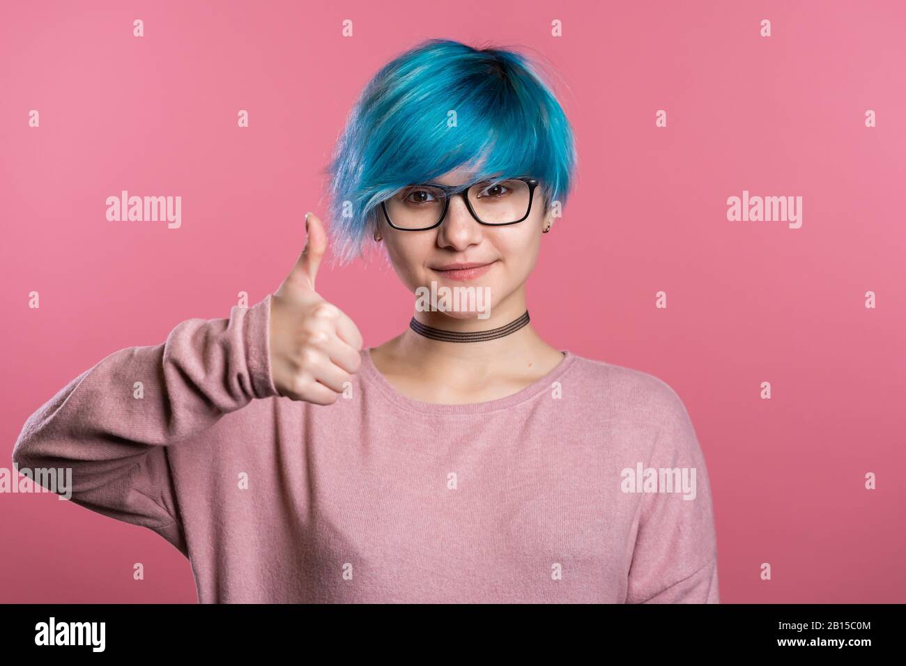 Young punk unusual woman with blue hair making thumbs up sign over pink ...