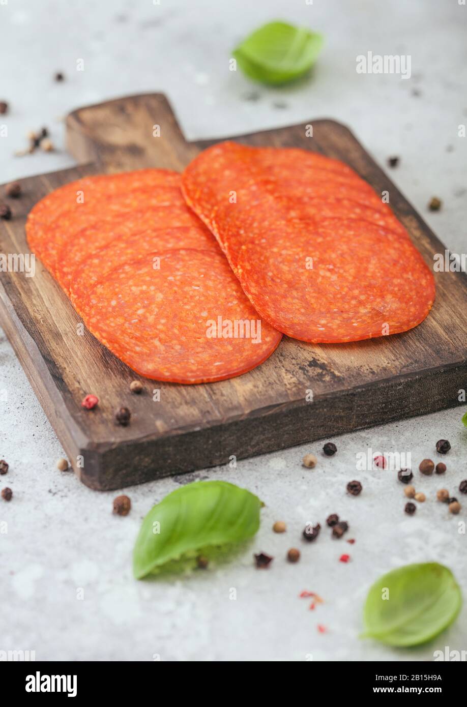 Spicy pepperoni salami with basil and pepper on wooden chopping board ...