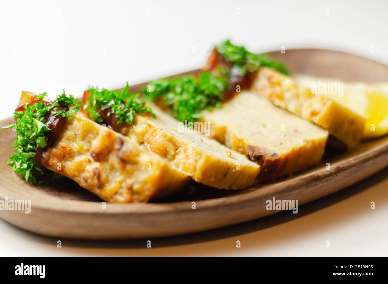 Cut potato cake served with sauce and parsley on a wooden plate ...