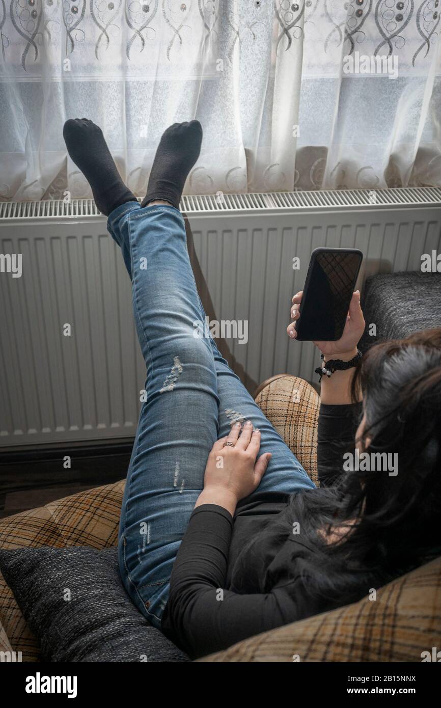 The girl sits on an armchair with her legs raised on the radiator ...