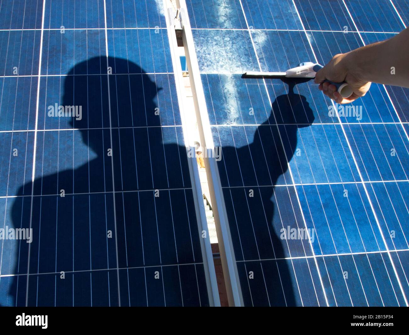 Hand and shadow cleaning solar panels with a glass cleaner wiper ...