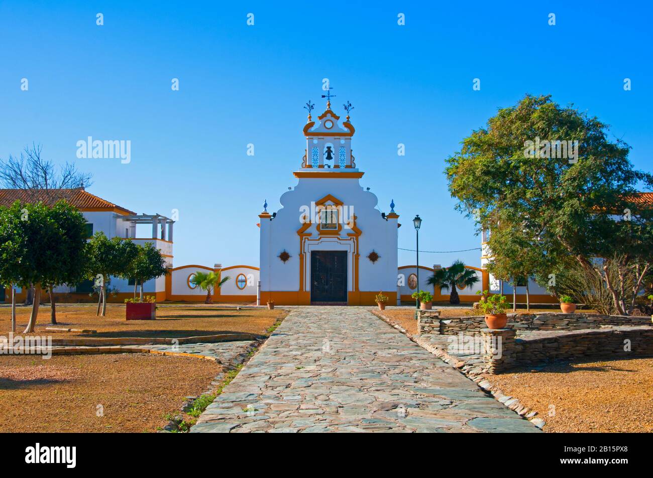 Small Spanish church in the park, trees and houses, clear blue sky ...