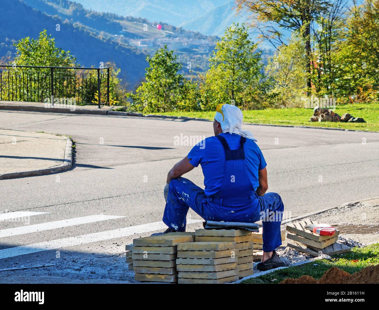 A man in work clothes sits on folded paving slab near the road Stock ...
