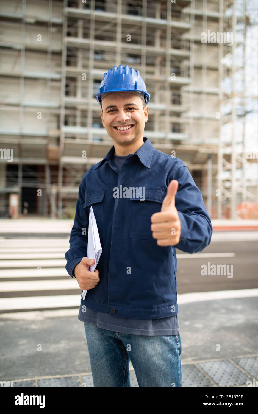Smiling site manager giving thumbs up in front of a construction site ...