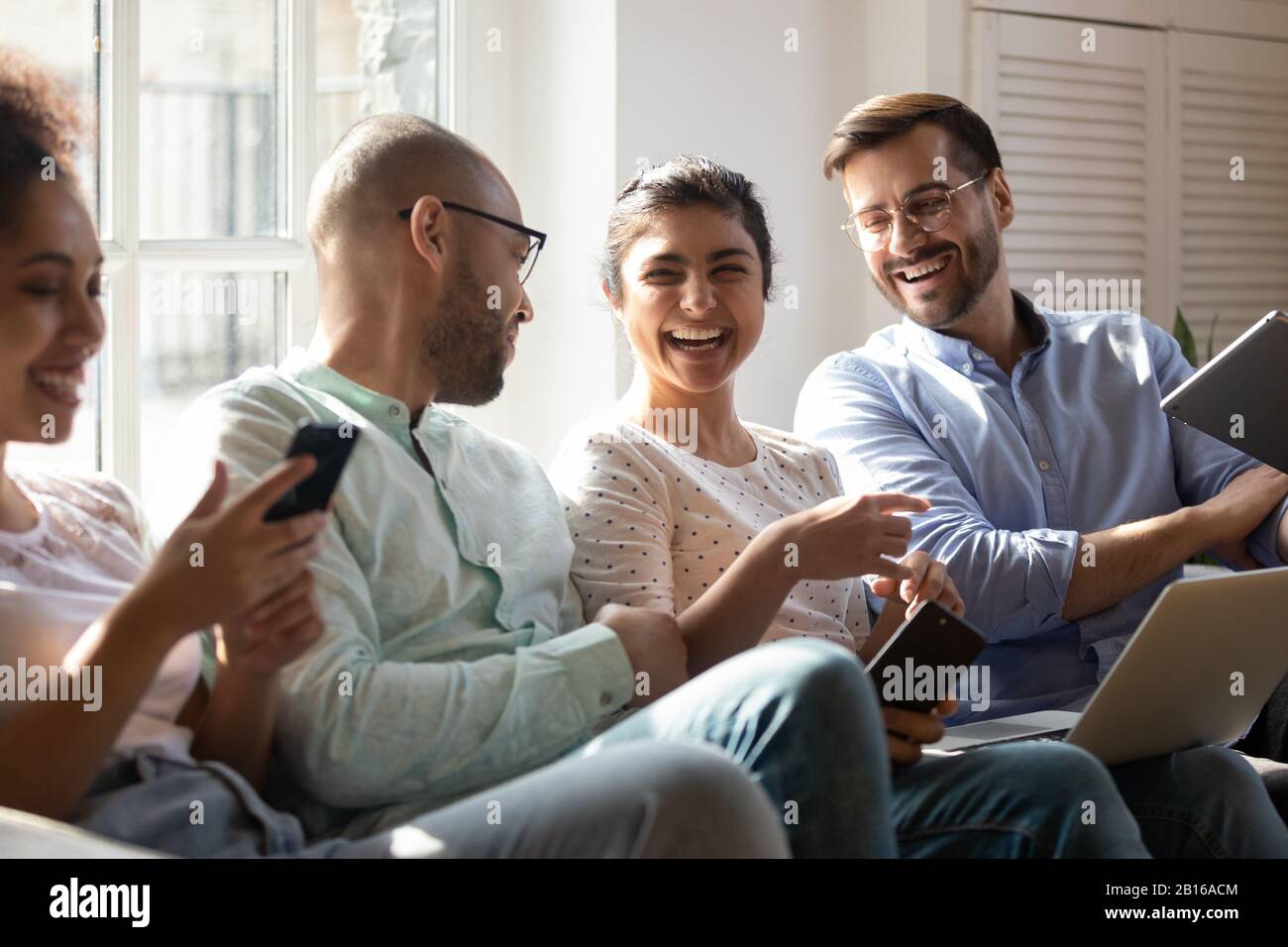 Diverse friends gathered together spend free time with modern devices ...