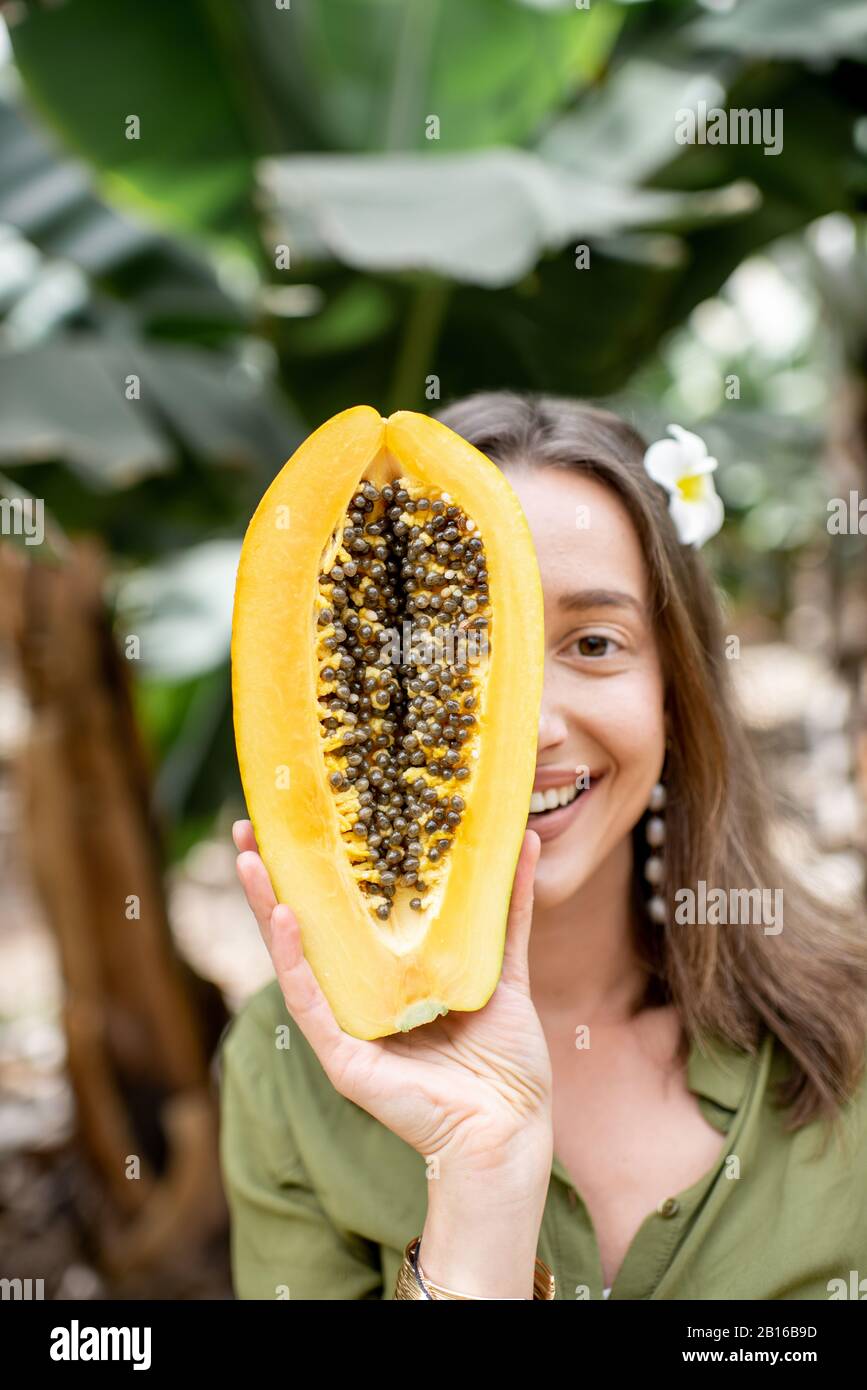 Closeup portrait of a young woman hiding her face behind sliced papaya ...