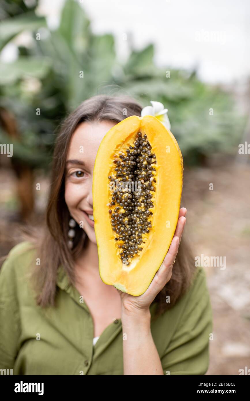Closeup portrait of a young woman hiding her face behind sliced papaya ...