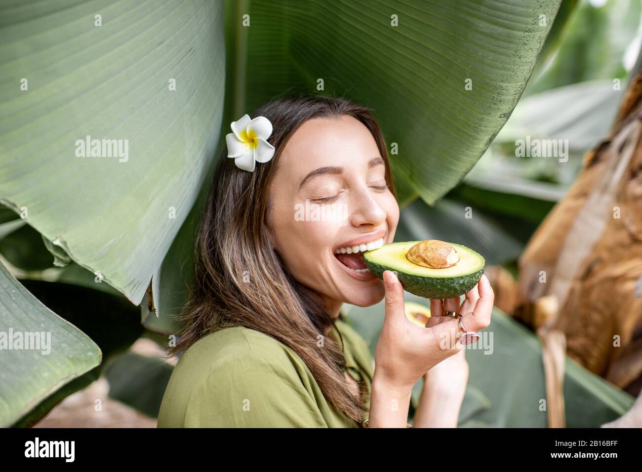 Young woman eating avocado berry in the banana leaves outdoors. Concept ...