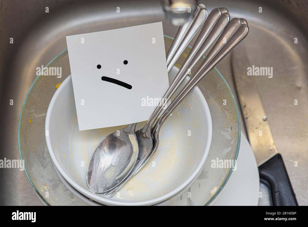 Some dirty dishes, spoons and knife in iron sink and paper with sad ...